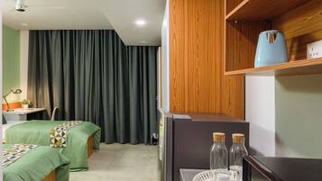 Quarto de hotel compacto com cozinha compacta, cama com roupa de cama verde, escrivaninha e uma grande janela com cortinas.