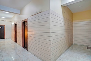 Um corredor com piso ladrilhado, porta de madeira e parede com painéis horizontais.