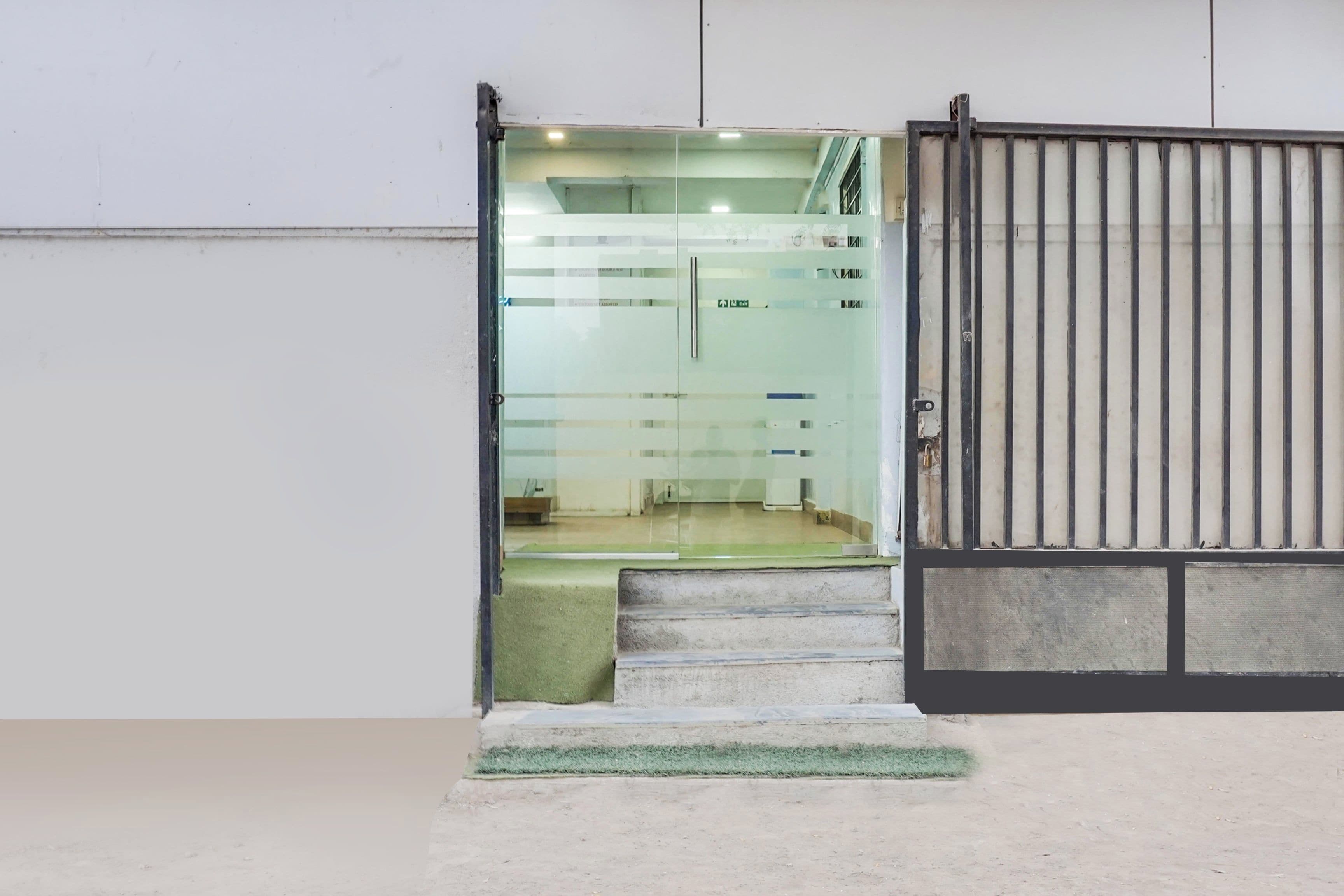 Entrada com porta de vidro e portão de metal, piso de concreto e um pequeno degrau até a porta.
