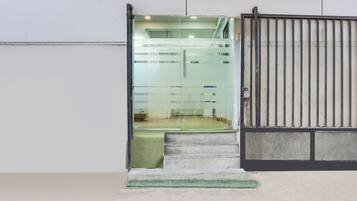 Entrada com porta de vidro e portão de metal, piso de concreto e um pequeno degrau até a porta.