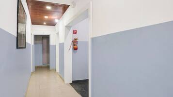 Um corredor com um extintor preso na parede, uma porta no final e um teto com vigas de madeira.