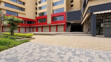 Edifício de vários andares com um pátio, apresentando fachada em vermelho e bege, um caminho pavimentado e uma pequena árvore.