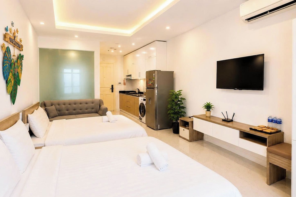 Quarto de hotel com duas camas, um sofá, uma área de cozinha e uma televisão.