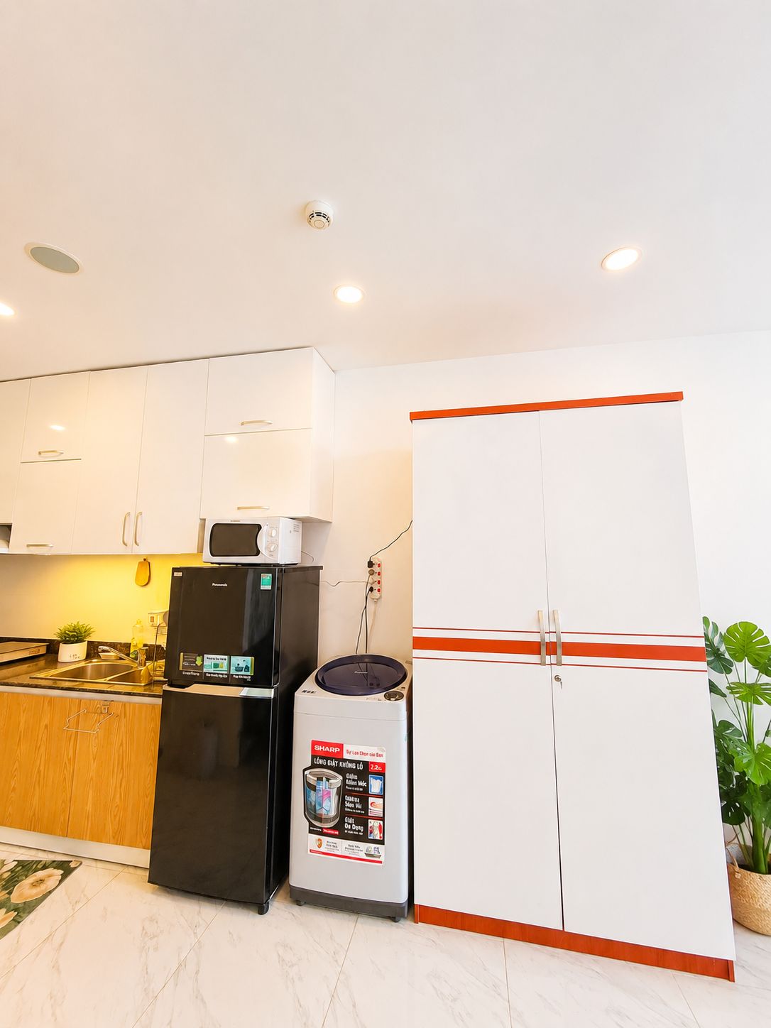 Cozinha compacta com armários brancos, geladeira preta, micro-ondas e dispenser de água.