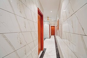 Um corredor com paredes e portas de mármore, que dá acesso a um quarto com ventoinha no teto.