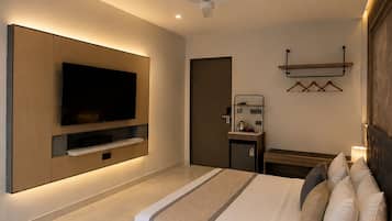Quarto de hotel moderno com uma TV de tela plana grande presa à parede, uma cama com cabeceira, mesas de cabeceira, uma escrivaninha e um ventilador de teto.