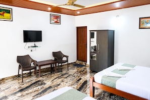 Quarto de hotel com cama, escrivaninha, duas cadeiras, televisão e guarda-roupa.