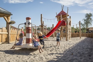Um parquinho de areia com um escorrega vermelho e uma estrutura de escalada de madeira.