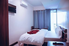 Quarto de hotel com uma cama, televisão na parede e janela com cortinas.