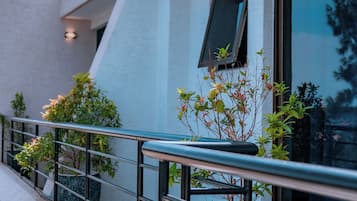 Um edifício moderno com uma grande janela de vidro, guarda-corpo metálico e alguma vegetação.