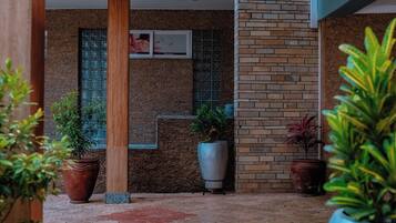 Uma área externa coberta com piso de azulejos, plantas em vasos e parede de tijolos.
