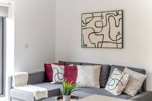 Uma sala de estar moderna com um sofá cinzento, uma poltrona branca e um vaso com planta.