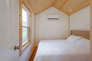 Quarto com teto de madeira, janela, cama com roupa de cama branca e ar condicionado.