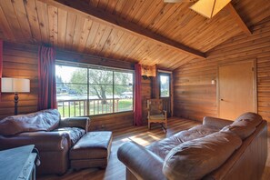 Interior de cabana de madeira com uma grande janela, sofás de couro e teto de madeira.