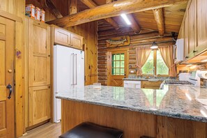 Interior de uma cabana de madeira com cozinha, incluindo geladeira, armários de madeira e bancada de granito.
