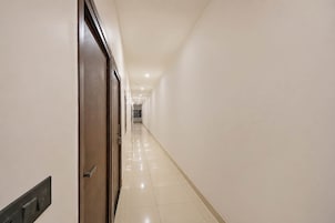 Um corredor com uma porta à esquerda, piso ladrilhado e teto com iluminação embutida.