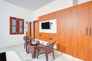 Quarto moderno com guarda-roupa de madeira, televisão fixada em parede de mármore, mesa de jantar com cadeiras e espaço para café.