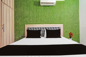 Quarto com cama, cabeceira, ar-condicionado fixado na parede e uma pequena planta em vaso.
