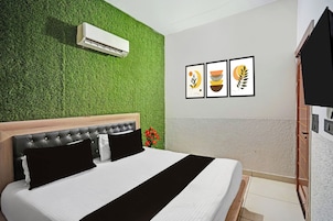 Quarto de hotel com parede verde, cama com roupa de cama preta e branca, e três quadros pendurados na parede.