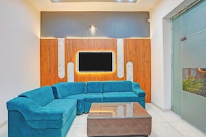 Sala de estar com sofá modular, mesa de centro, televisão de tela plana fixada em parede de madeira com detalhes em mármore, e porta de vidro deslizante que dá para uma varanda.