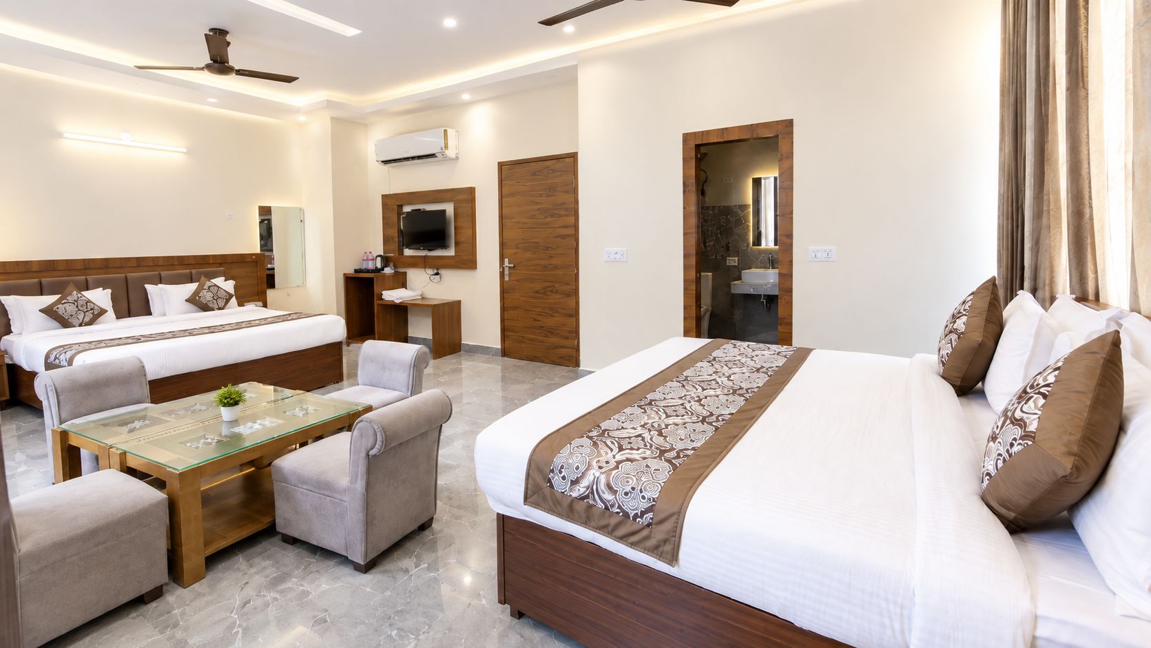 Quarto de hotel com uma cama grande, uma cama menor, um sofá, uma mesa com tampo de vidro e uma televisão.