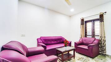 Quarto com ventoinha no teto, janela com cortinas estampadas e móveis roxos.