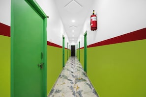 Um corredor com paredes verdes e vermelhas, piso de mármore e um extintor fixado na parede.