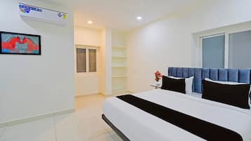 Quarto de hotel com cama, janela, mesa de cabeceira com um vaso e ar-condicionado fixado na parede.