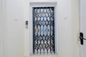 Uma porta com grade de metal preta, um interruptor de luz e um leitor de cartão-chave na parede.