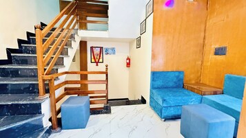 Um hall de hotel com escadaria de madeira, área de estar azul e um extintor de incêndio na parede.