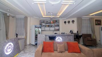 Uma sala de estar moderna com sofá, espaço de bar com garrafas de bebidas e geladeira.