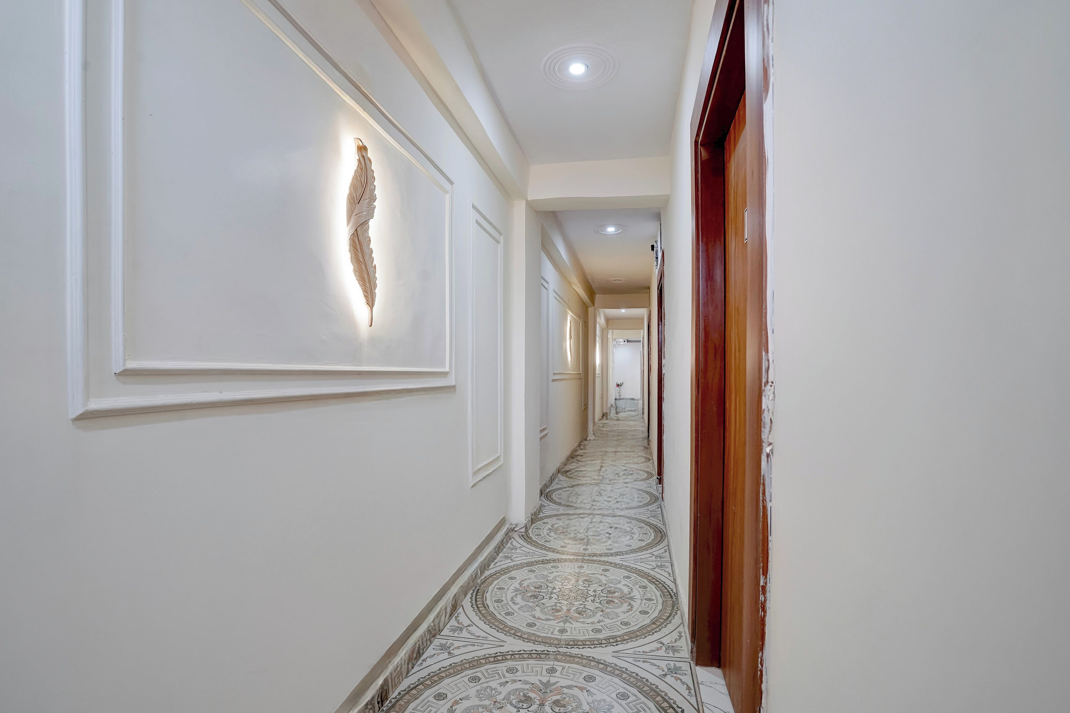 Um corredor com piso estampado, um detalhe decorativo na parede e uma porta de madeira.
