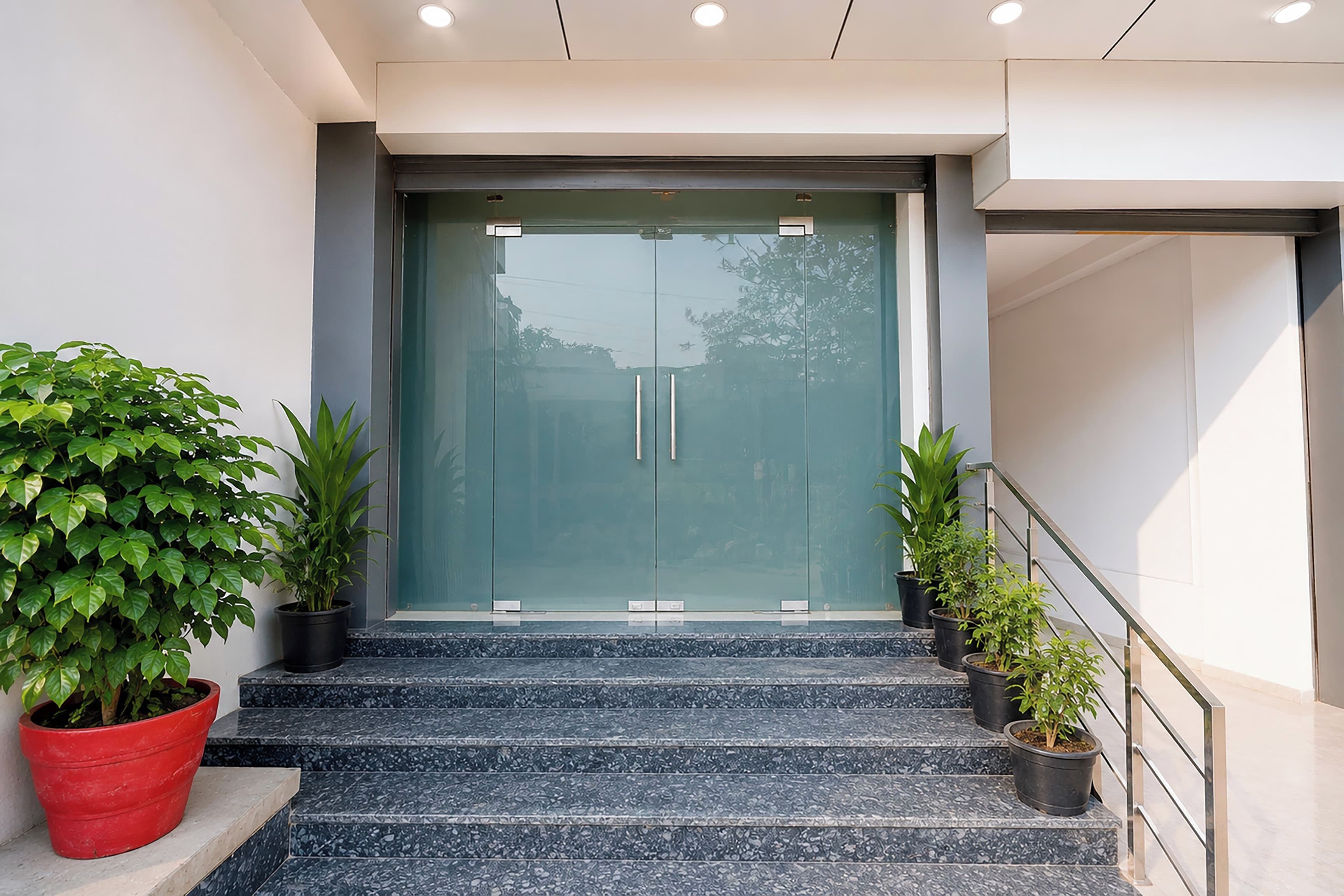 Entrada de um edifício moderno com porta de vidro, degraus de mármore e plantas em vasos.