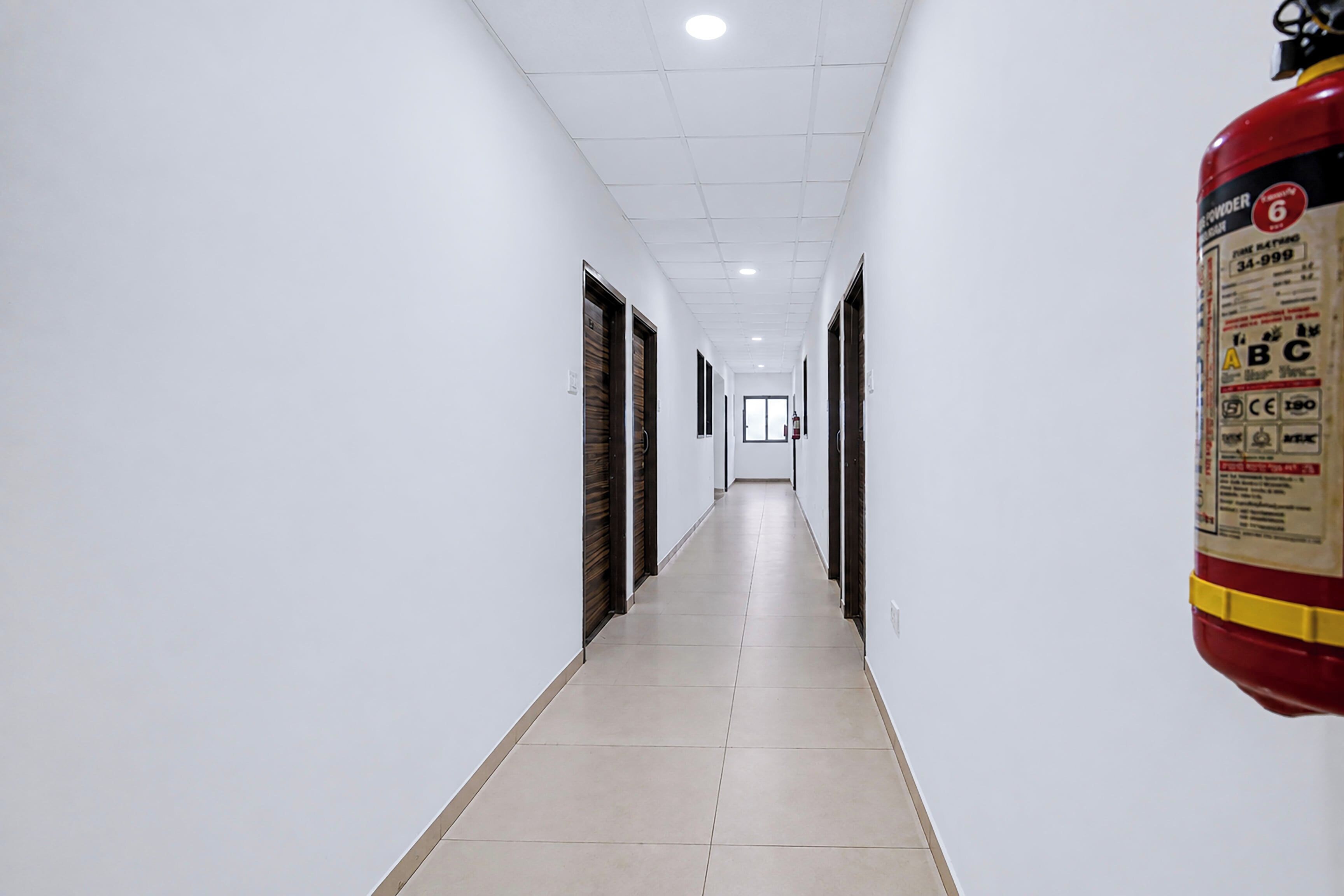 Um corredor com paredes brancas, um extintor fixado na parede e uma porta no final.