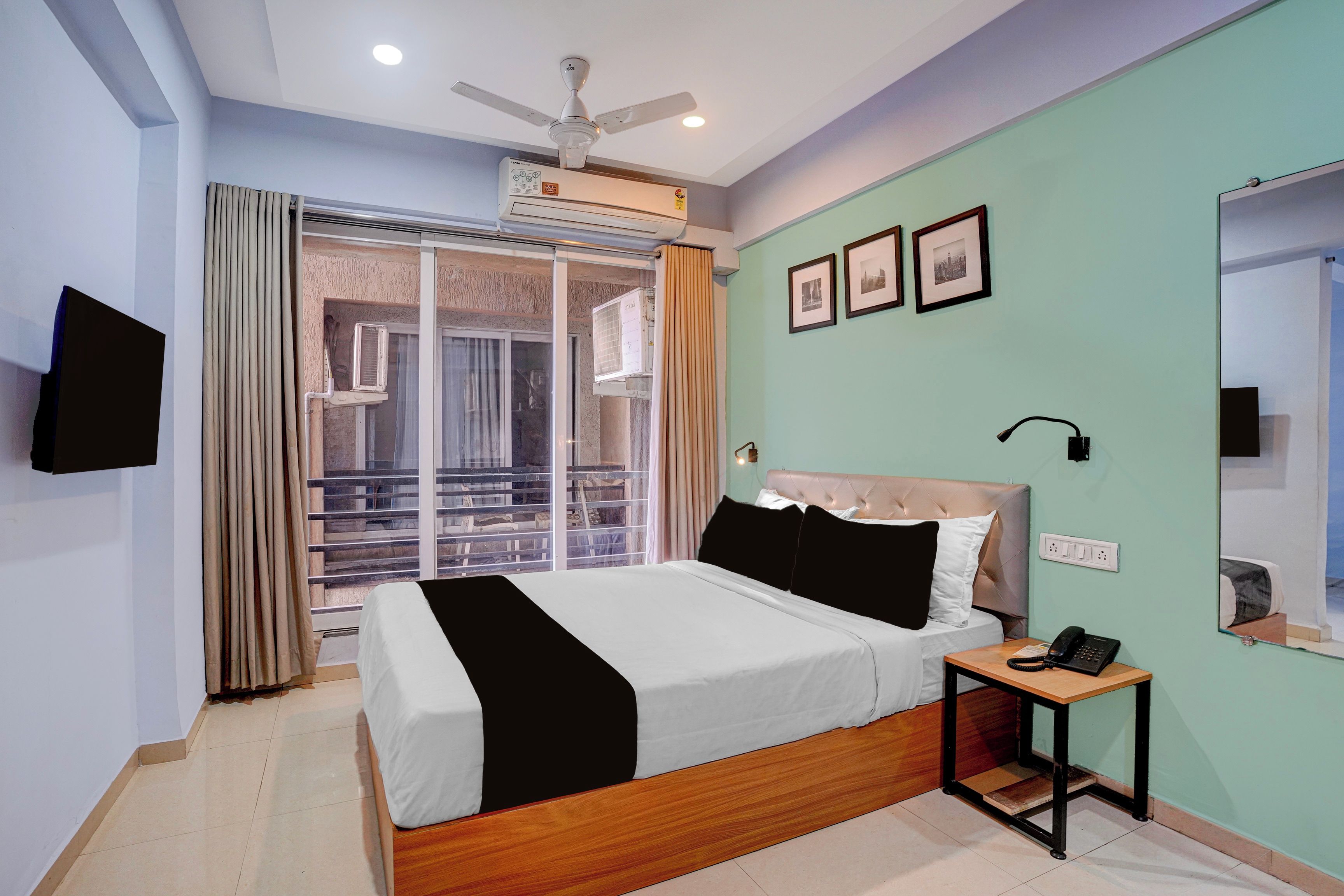 Quarto de hotel com cama, mesa de cabeceira com telefone, ventoinha no teto e janela com cortinas.