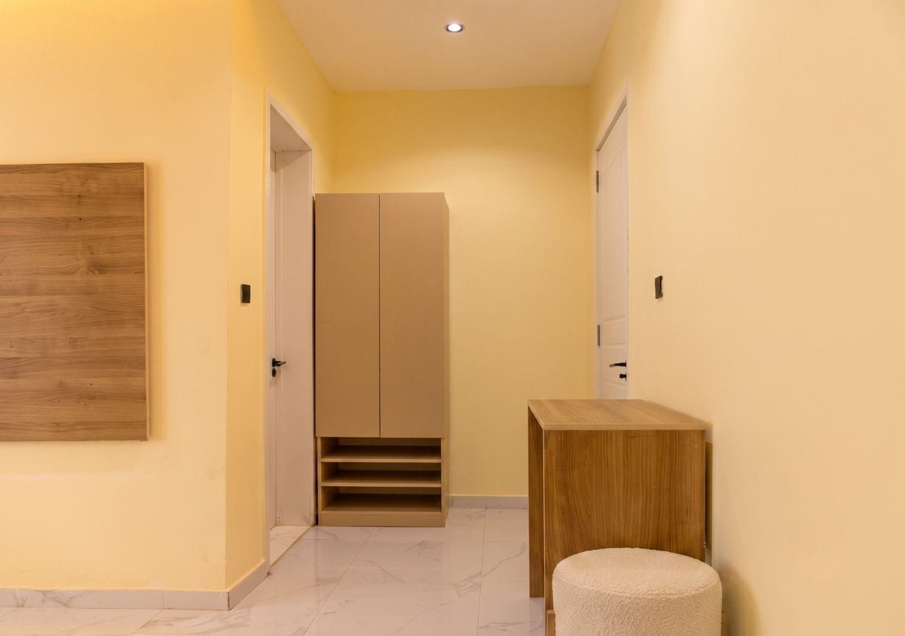 Um corredor com um guarda-roupa, uma mesinha e um banco.