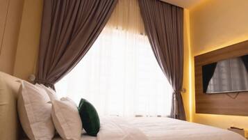 Quarto de hotel com cama, cortinas, televisão na parede e janela com cortinas leves.