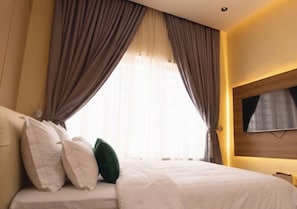 Quarto de hotel com cama, cortinas, televisão na parede e janela com cortinas leves.