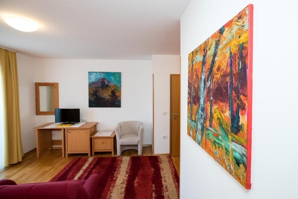 Quarto com cama, escrivaninha com computador, cadeira e duas pinturas na parede.