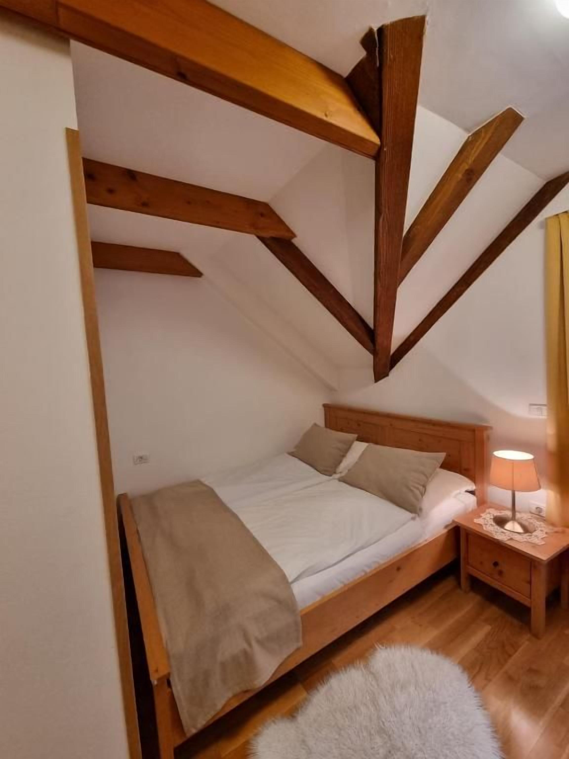 Quarto com cama de madeira, mesa de cabeceira com abajur e tapete macio no chão.