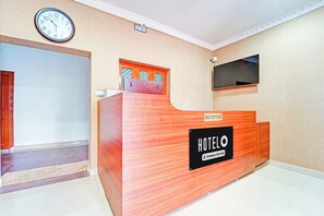 Uma receção de hotel com um relógio acima, um letreiro de receção e uma televisão na parede.