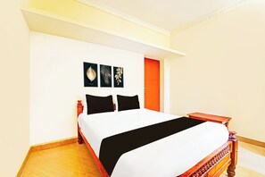 Quarto com cama, mesa de cabeceira, piso de madeira e uma porta.