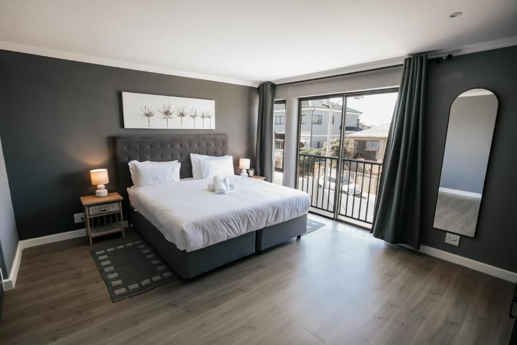 Quarto de hotel moderno com uma cama grande, uma mesinha de cabeceira, janela com vista e espelho na parede.