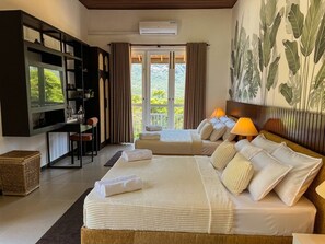 Quarto de hotel com duas camas, uma mesa, uma cadeira e uma janela grande com cortinas.