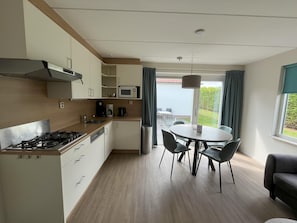 Cozinha moderna com fogão a gás, micro-ondas e cafeteira, que dá acesso a uma sala de jantar com mesa e cadeiras.