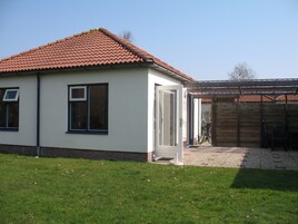 Uma casa térrea com telhado de telhas, porta da frente e pequeno jardim frontal.