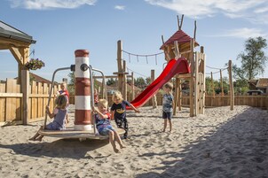 Um parquinho de areia com um escorrega vermelho e uma estrutura de escalada de madeira.