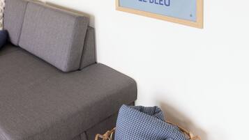 Um quarto com um sofá cinzento, uma obra de arte emoldurada com o texto 'LE BLEU' e uma peça pequena emoldurada com um design abstrato.