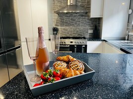 Uma bancada de cozinha com uma garrafa de champanhe, duas taças e uma bandeja de doces e morangos.
