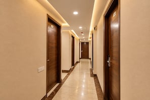 Corredor de hotel com portas de madeira numeradas 105 e 103, piso de mármore e iluminação embutida no teto.